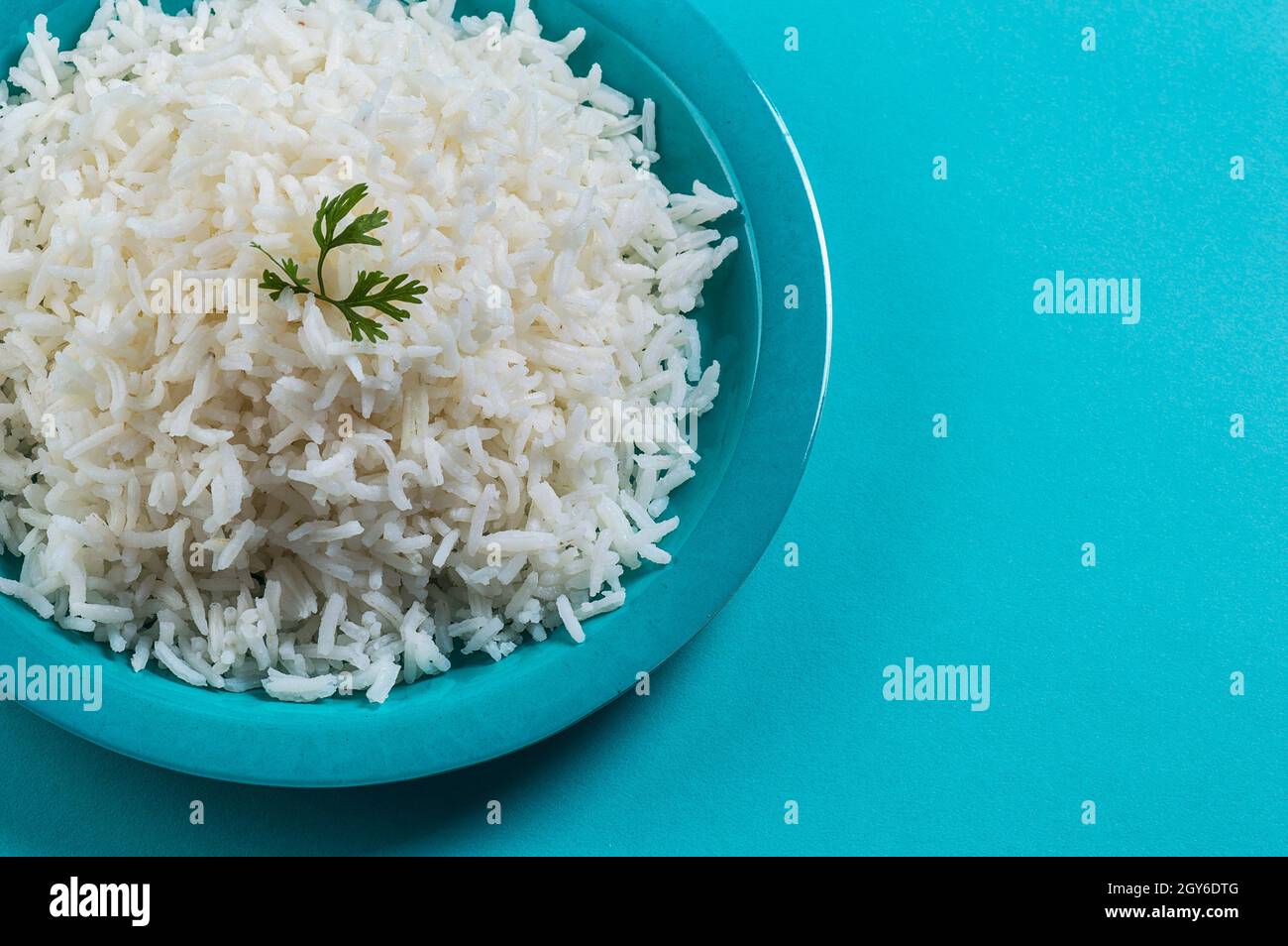 Cooked plain white basmati rice with corriander in a blue plate on blue ...