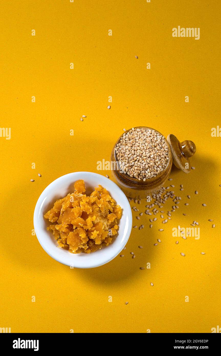 Sesame Seeds in clay pot with Jaggery in bowl on yellow background ...