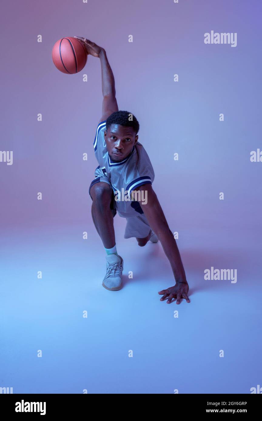 Muscular basketball player with ball shows his skill in studio, neon ...