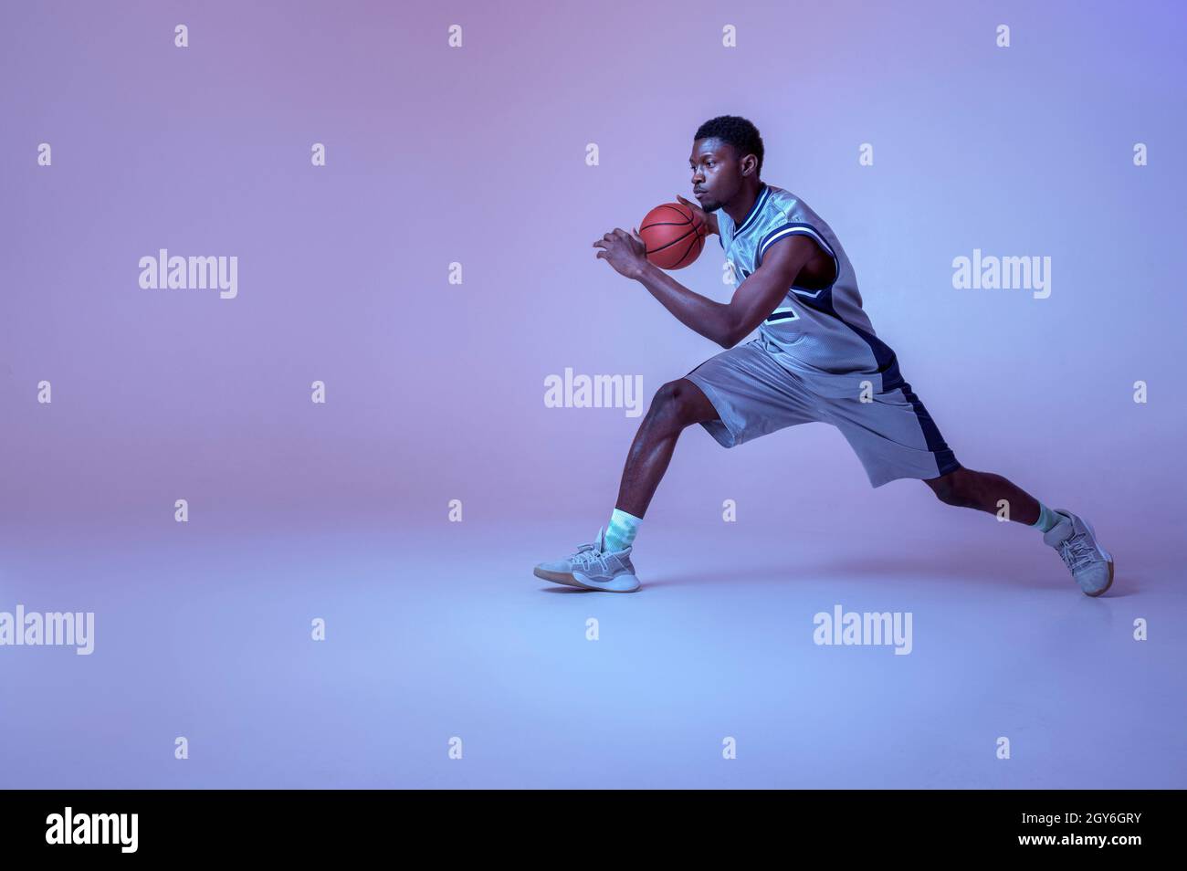 Basketball player practicing with ball in studio, neon background ...