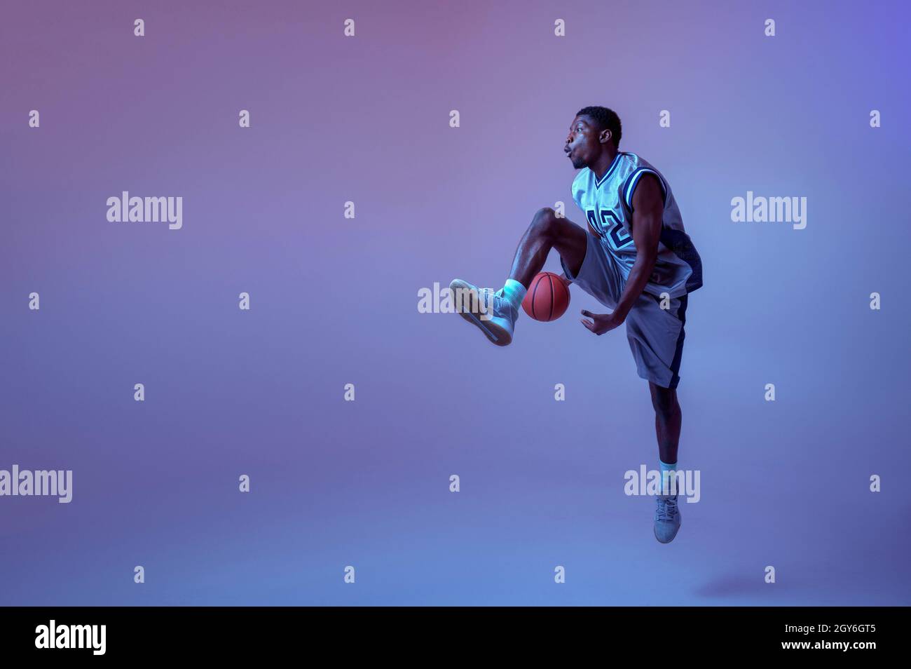 Basketball player practicing with ball in studio, neon background ...