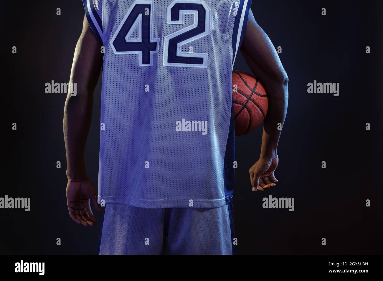 Basketball player poses with ball in studio, back view, black ...