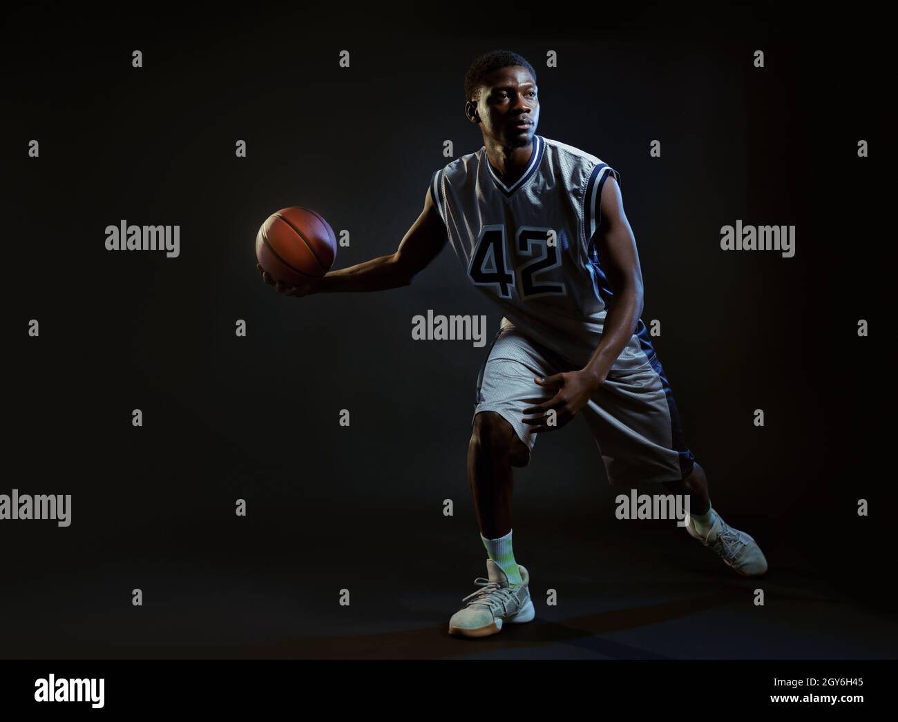 Muscular basketball player with ball shows his skill in studio, black ...