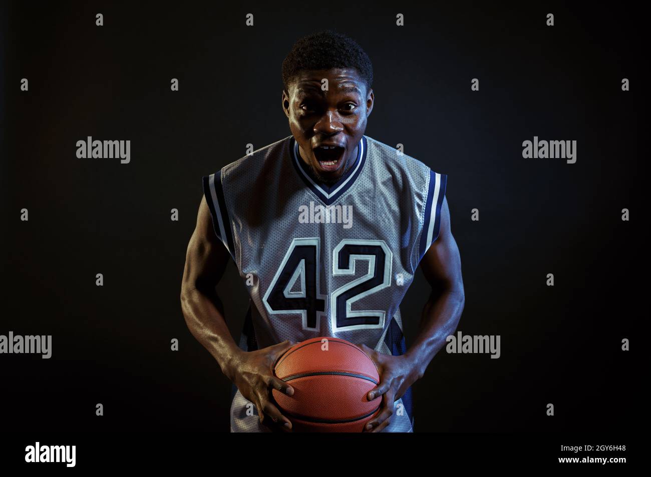 Aggressive basketball player poses with ball in studio, black ...