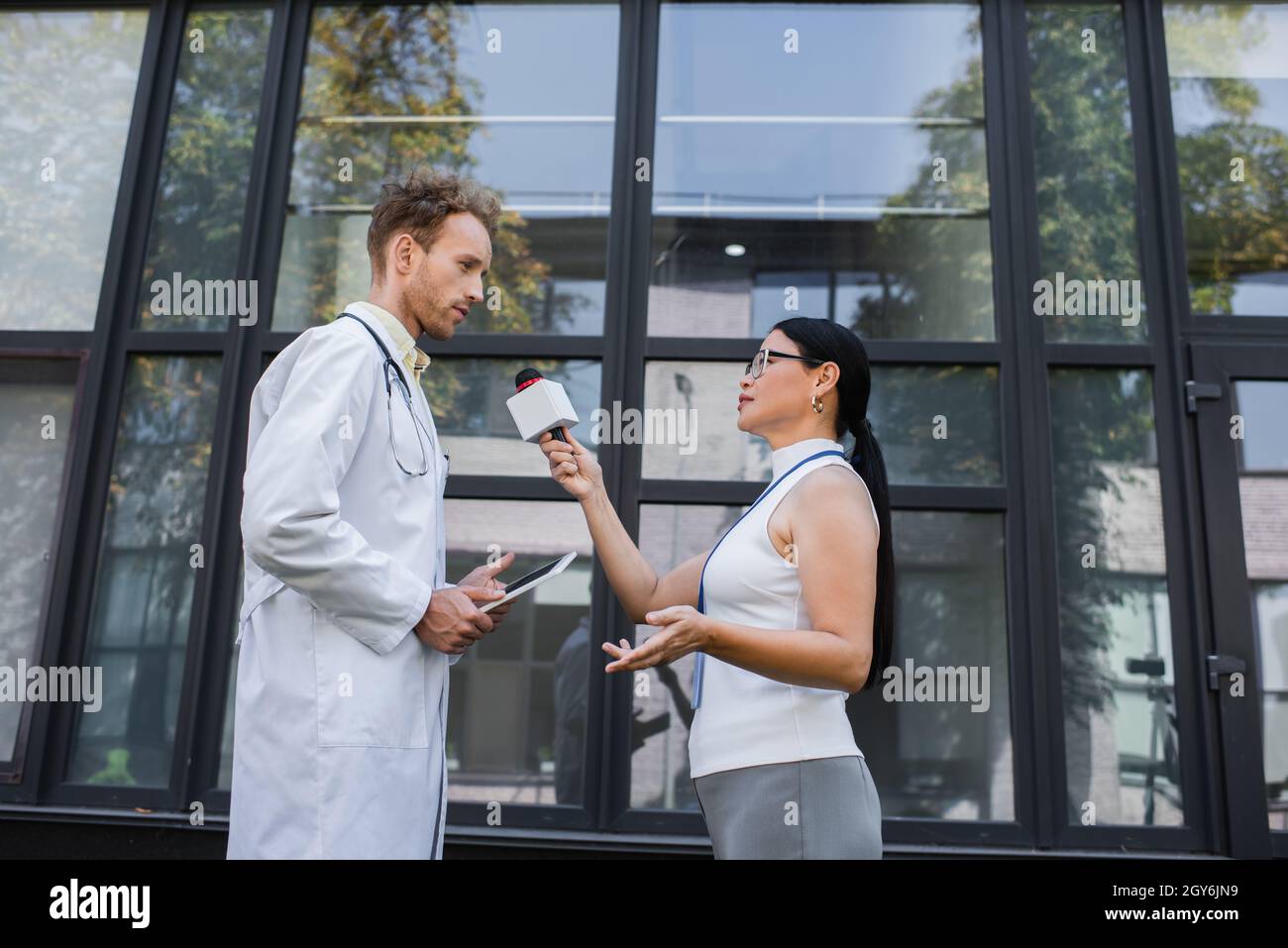 side view of asian journalist holding microphone while taking interview ...