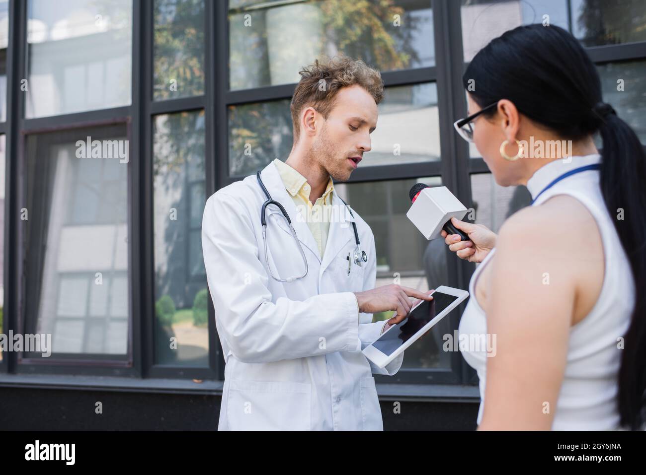 doctor in white coat pointing at digital tablet while giving interview ...