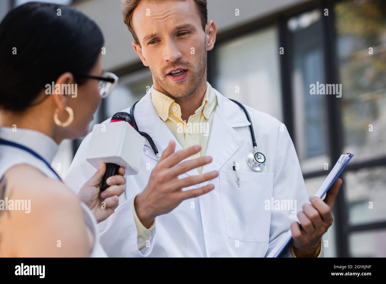 doctor in white coat holding clipboard and gesturing while giving ...