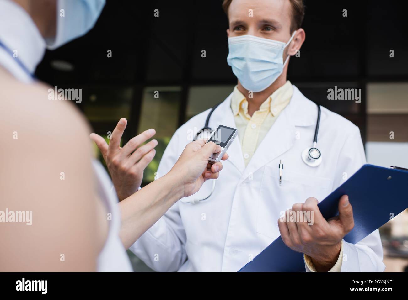 blurred reporter holding voice recorder near doctor in medical mask and ...