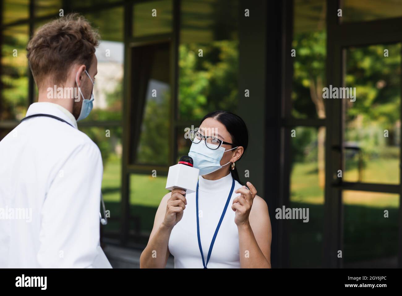 asian reporter in medical mask talking in microphone near doctor in ...