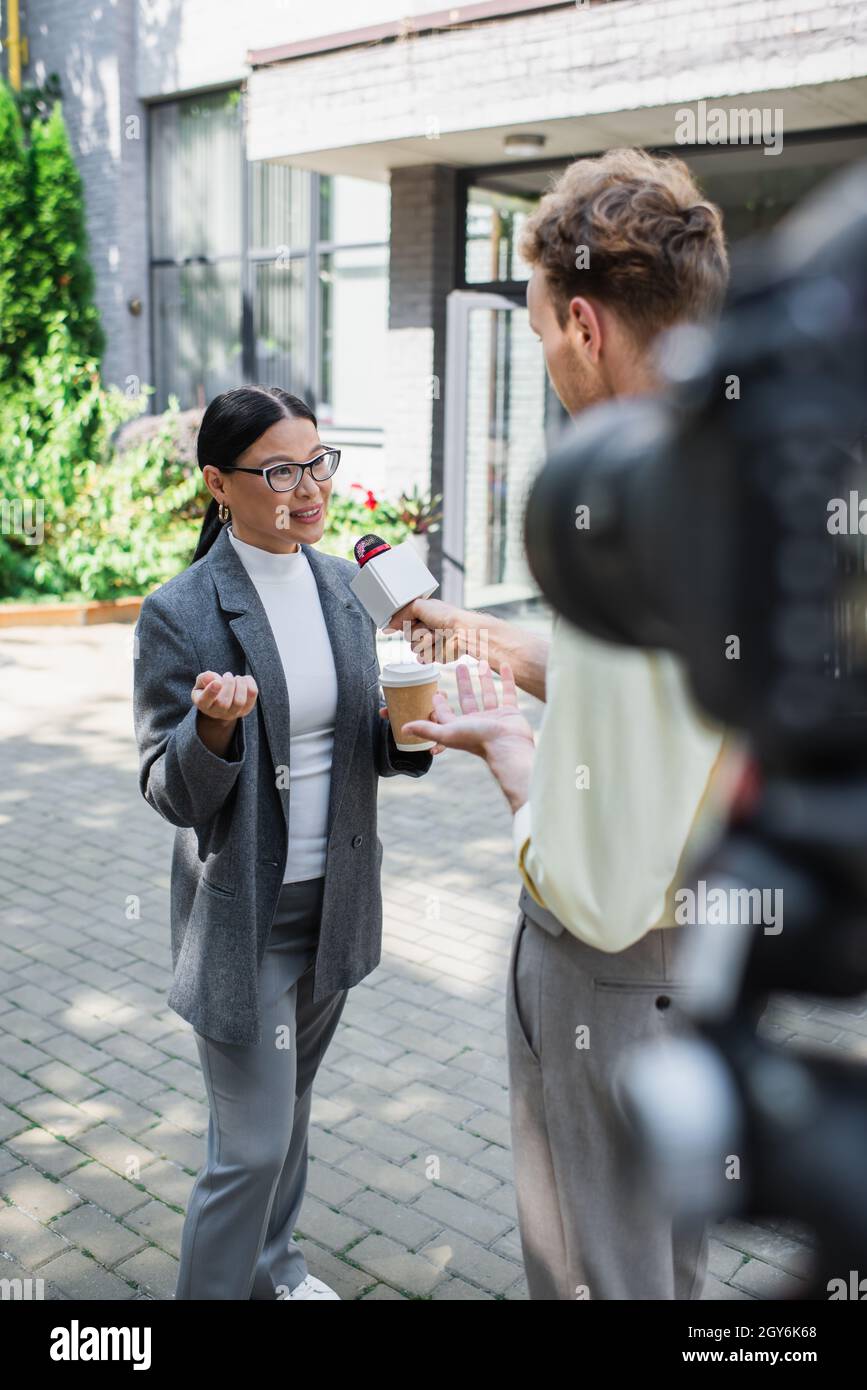 reporter holding microphone near cheerful asian businesswoman with ...