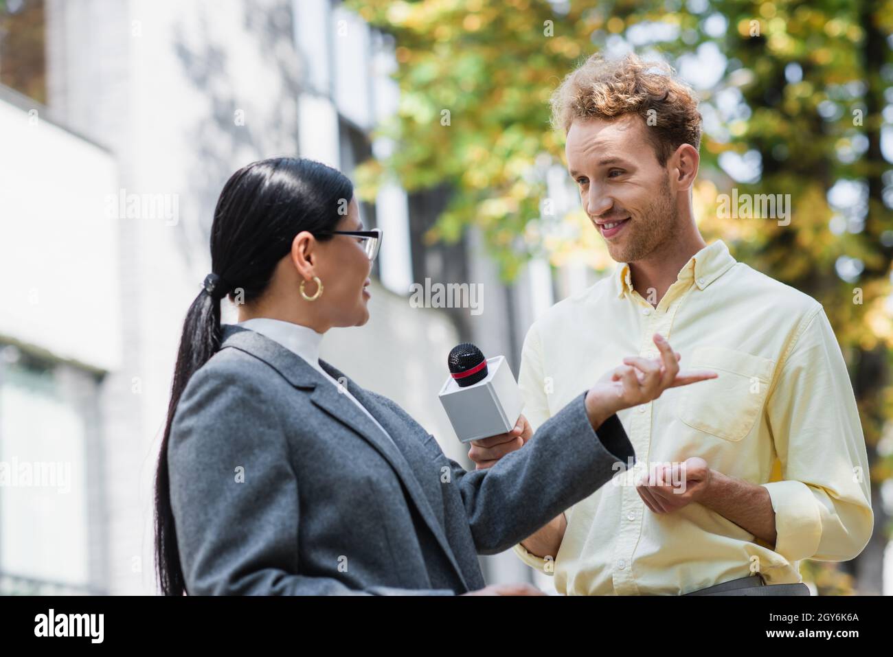 cheerful reporter holding microphone near asian businesswoman pointing ...
