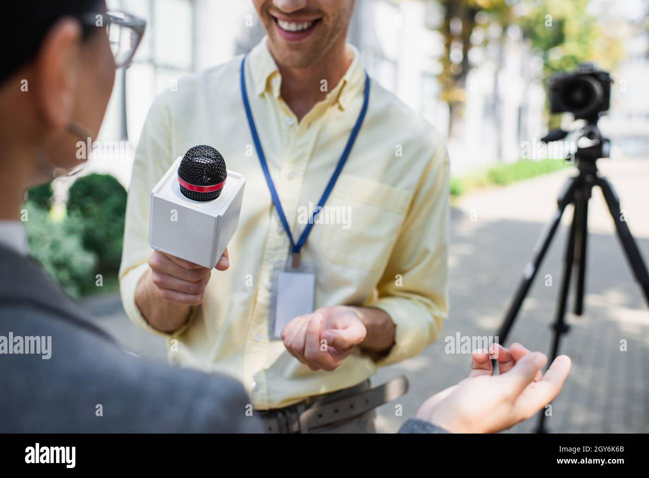 cheerful reporter holding microphone near blurred businesswoman ...