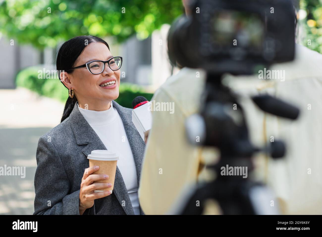 blurred reporter holding microphone near happy asian businesswoman with ...