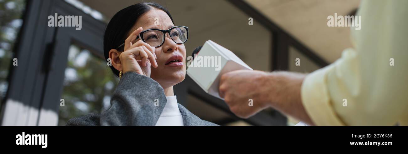 low angle view of reporter with microphone near pensive asian ...