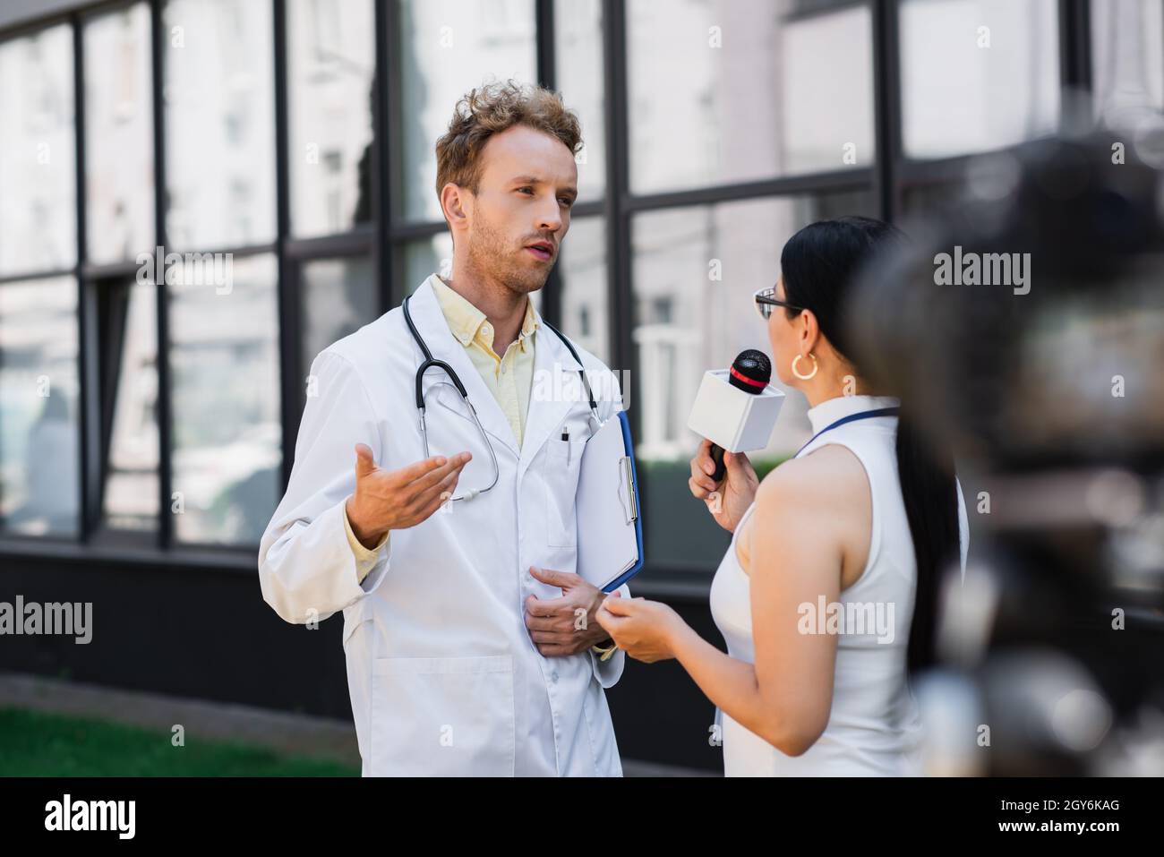 doctor in white coat gesturing while giving interview to asian ...