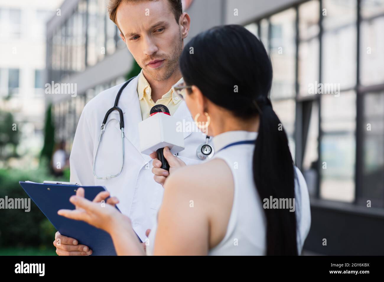 doctor in white coat holding clipboard and looking at blurred ...
