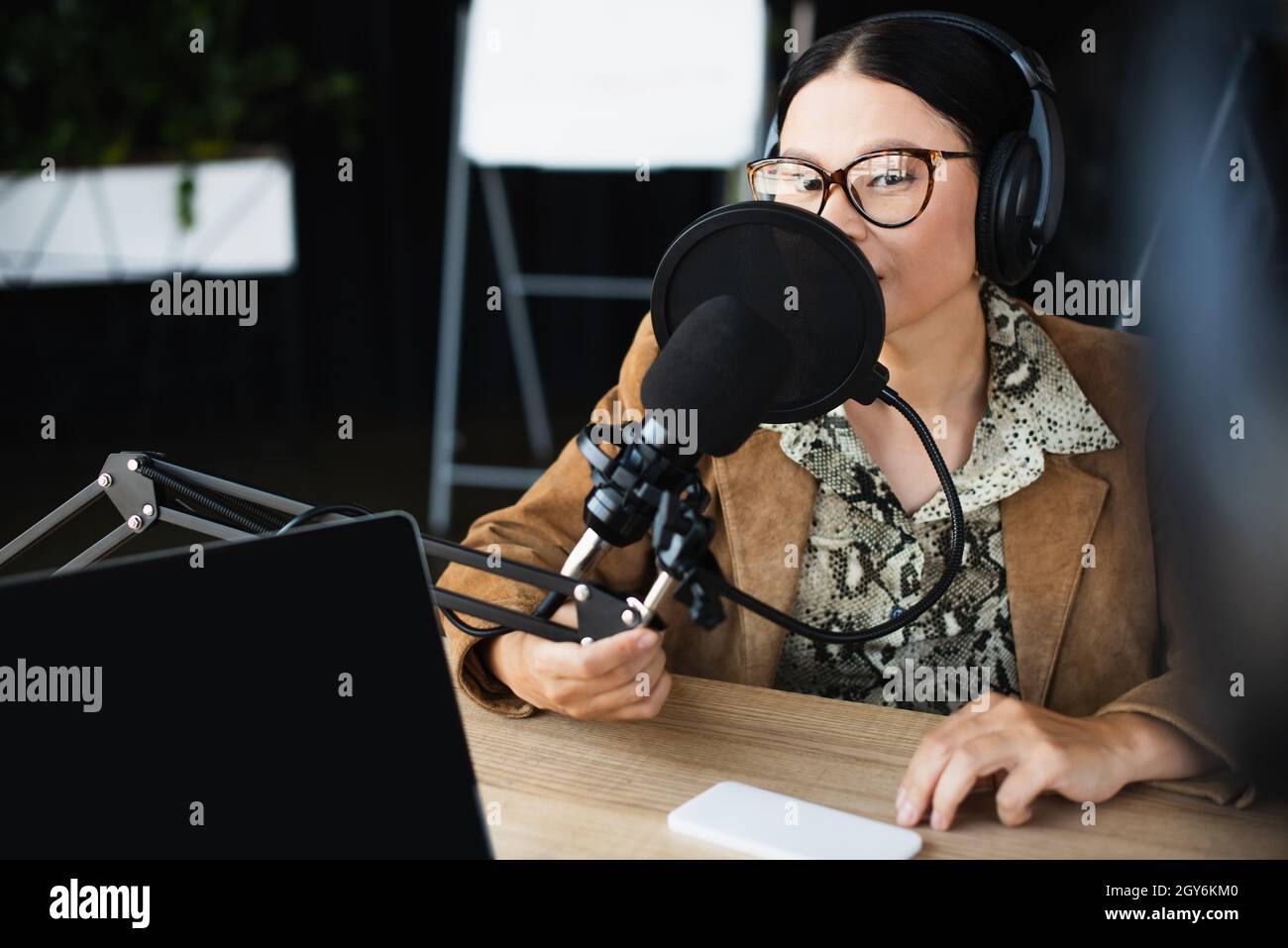 asian radio host in glasses and headphones talking near gadgets in ...