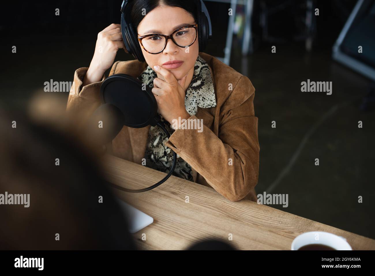 thoughtful asian radio host in glasses and headphones looking at ...