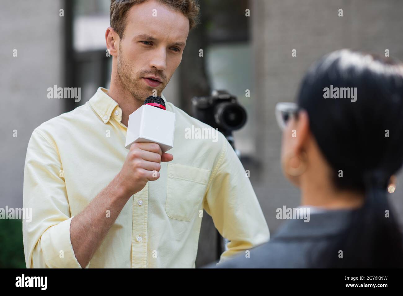reporter holding microphone and talking near blurred businesswoman ...