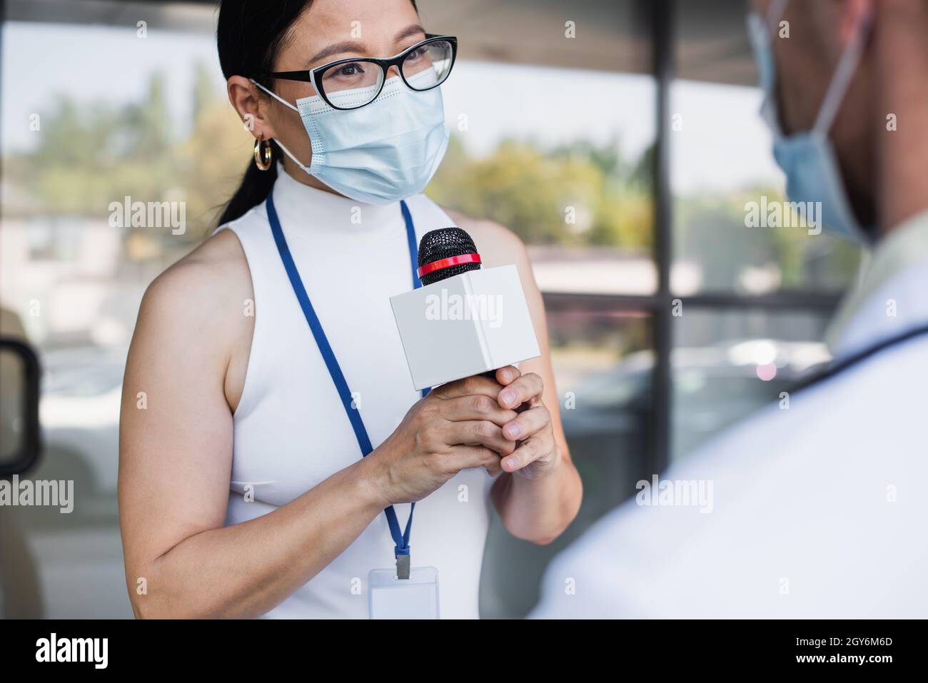 asian reporter in glasses and medical mask talking in microphone near ...