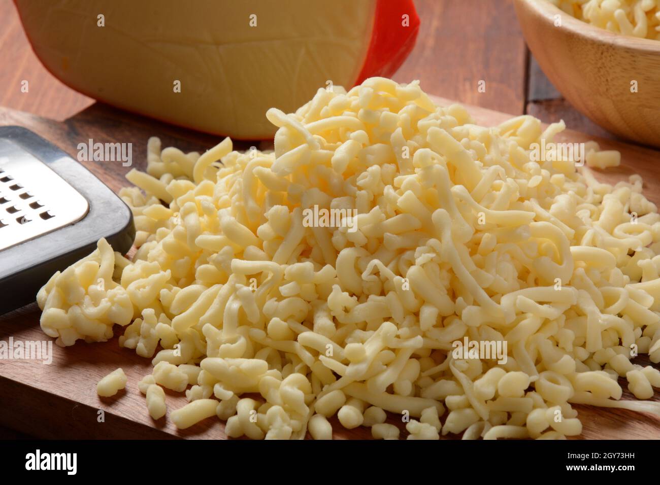 Heap of shredded cheese on small wooden board. Grated cheese for ...