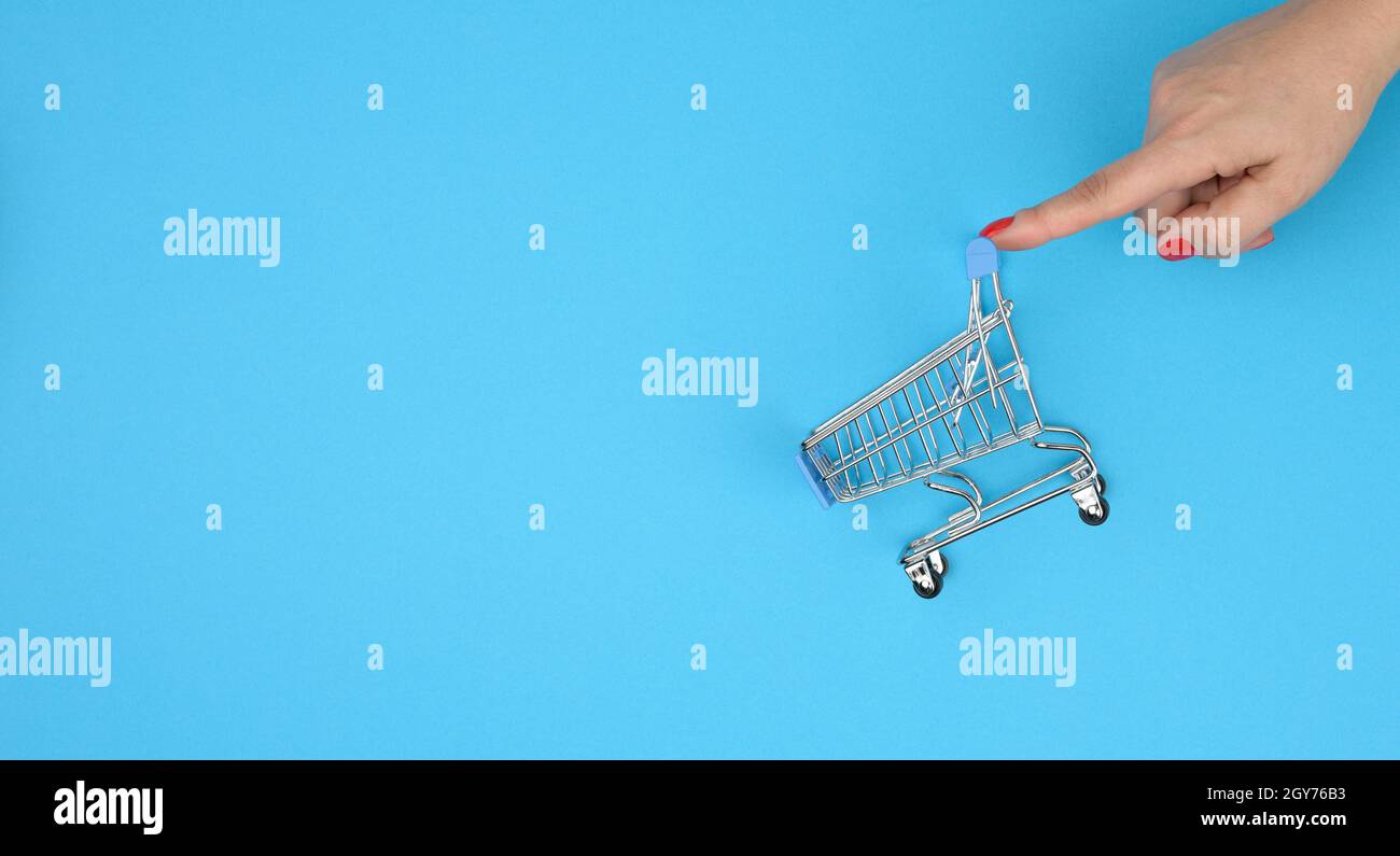 female hands hold an empty metal miniature trolley on a blue background ...