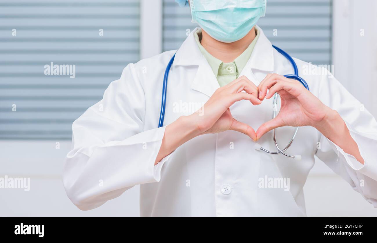 Closeup of doctor woman wearing white coat standing making heart finger ...