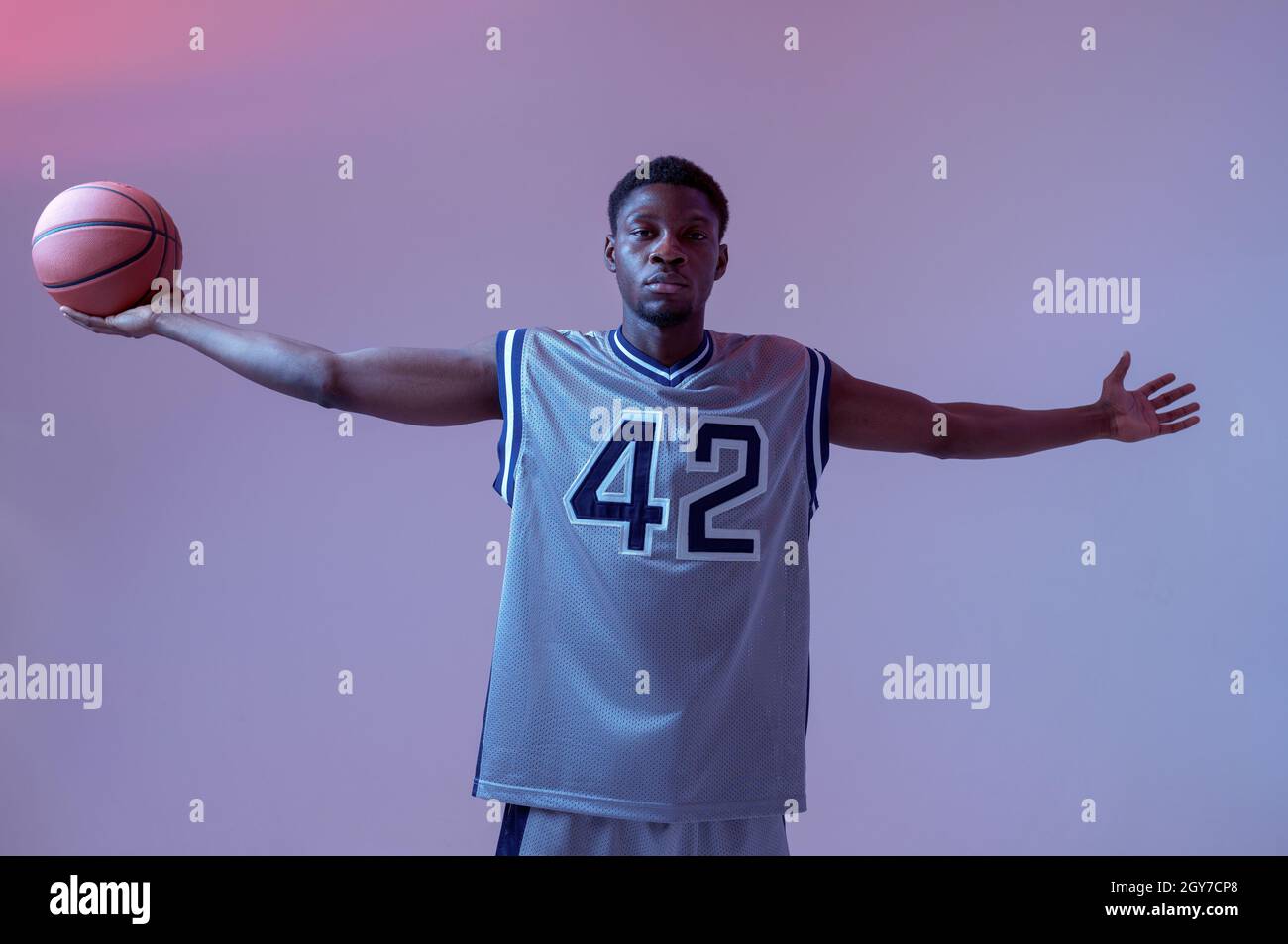 Athletic basketball player poses with ball in studio, neon background ...