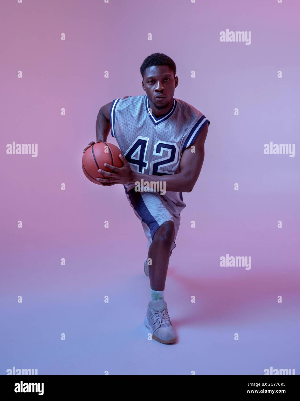 Basketball player practicing with ball in studio, neon background ...