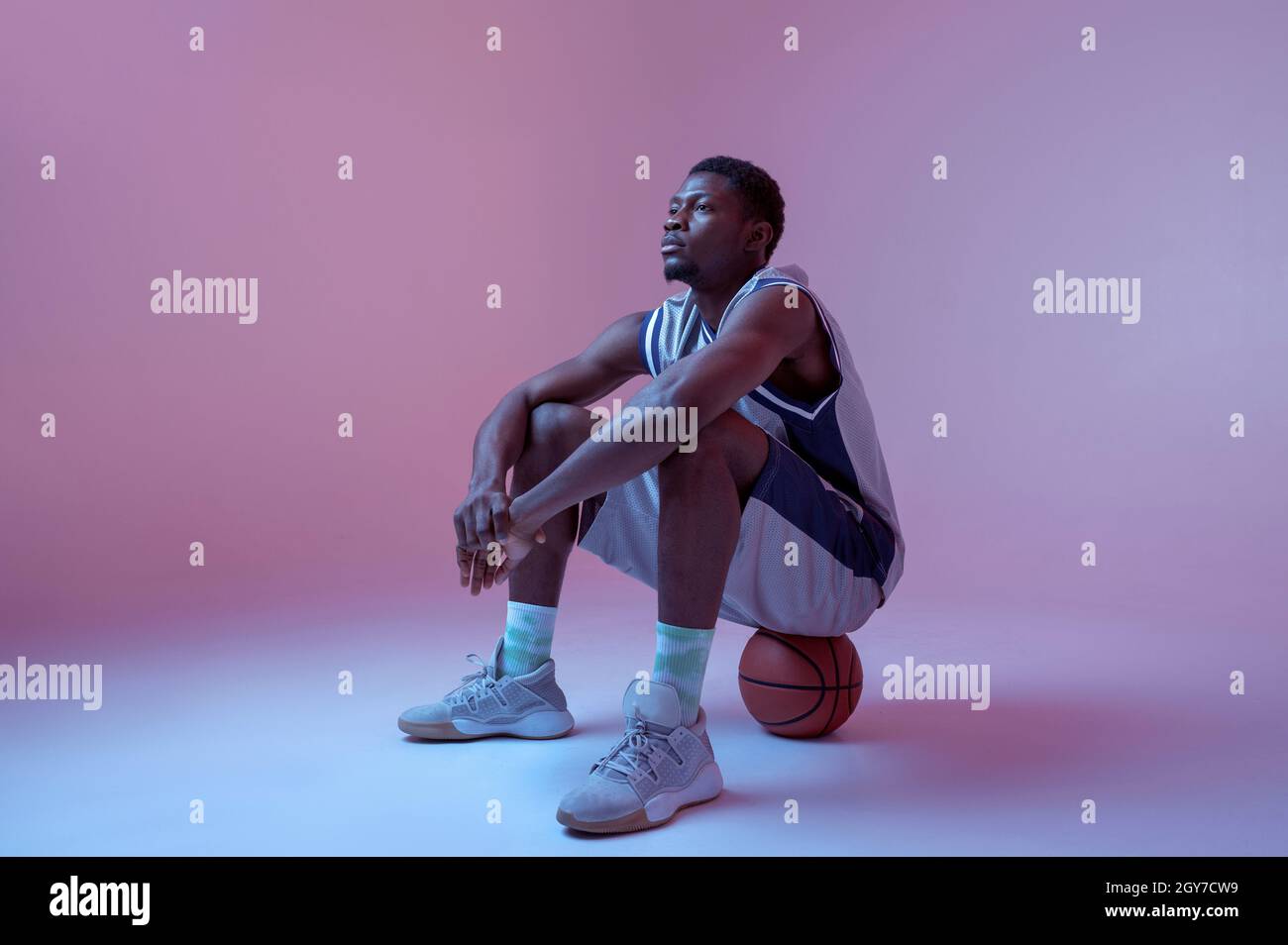 Basketball player sitting on ball in studio, neon background ...