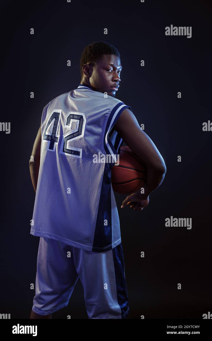 Basketball player poses with ball in studio, back view, black ...