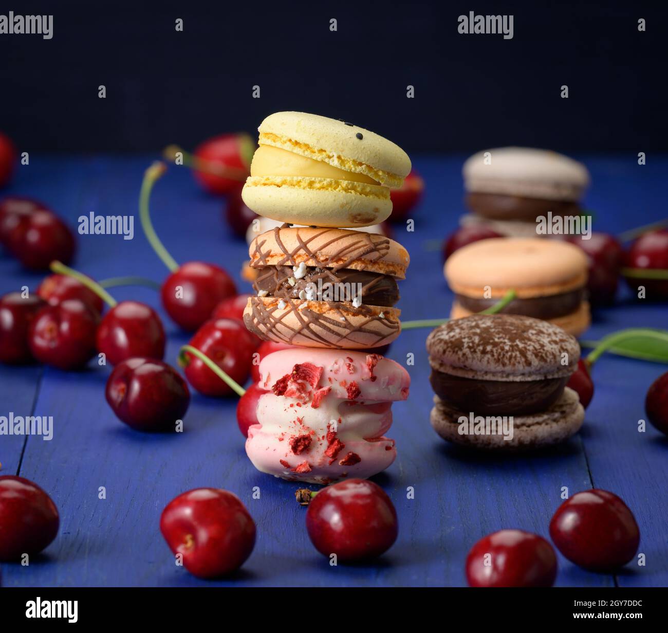 stack of multicolored macarons and ripe red cherries on blue wooden background Stock Photo - Alamy
