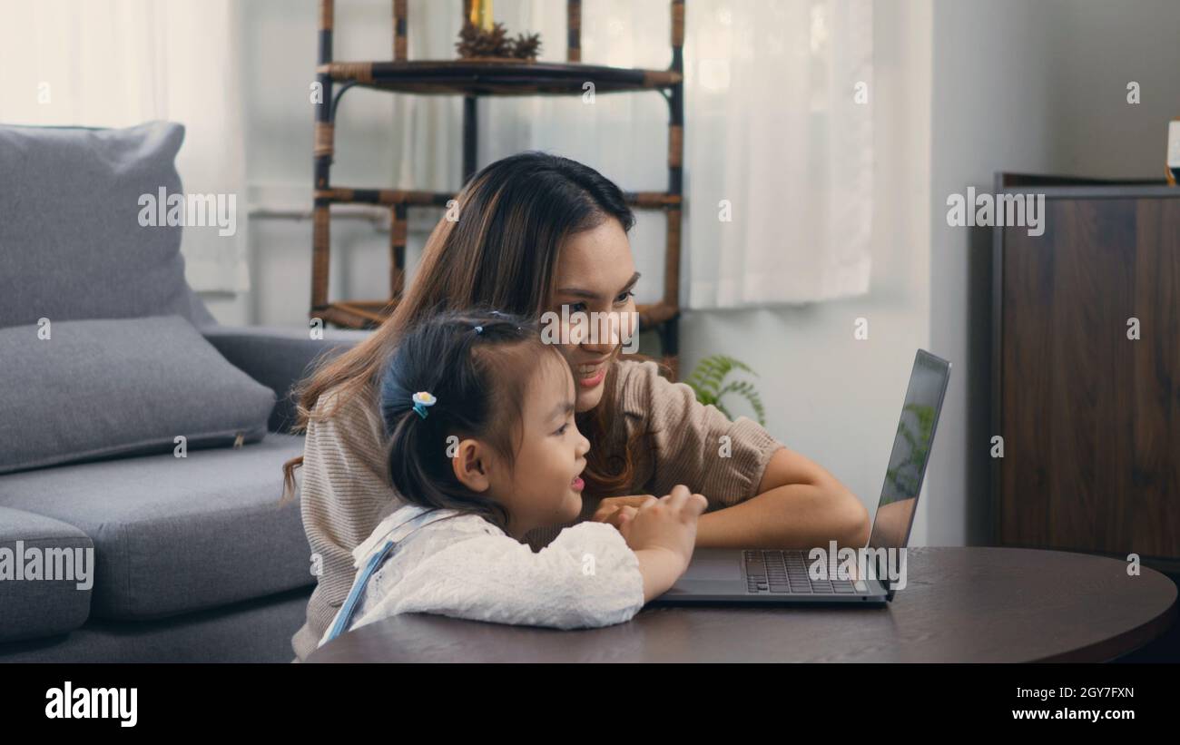 Asian young mother with laptop computer teaching her kid to learn or ...