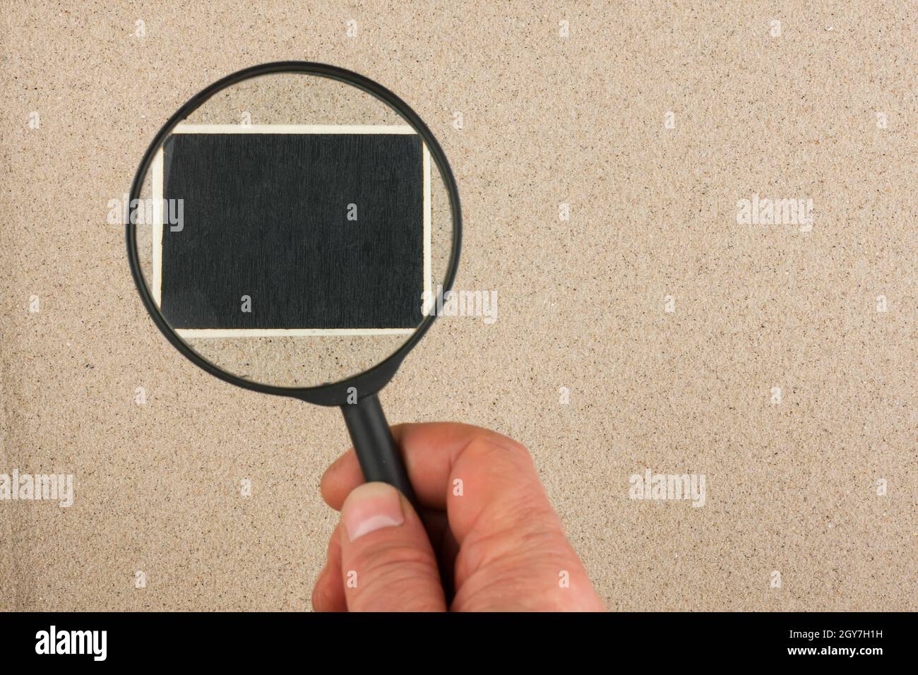 Hand with magnifying glass over the sign, in the sand, with space for ...