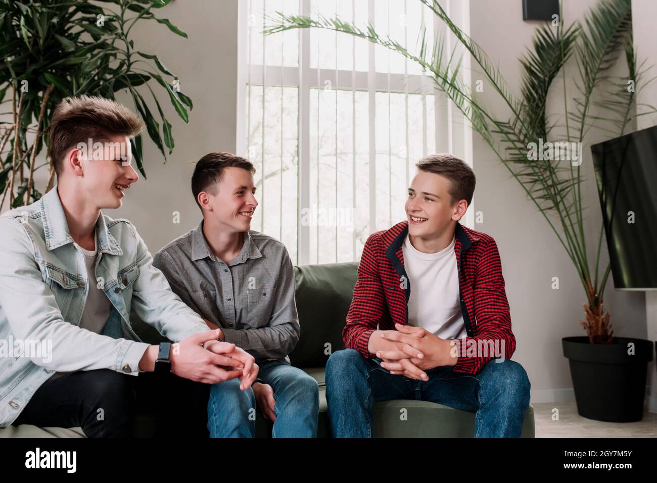 Three male friends are talking at the green sofa in living room. Guys ...