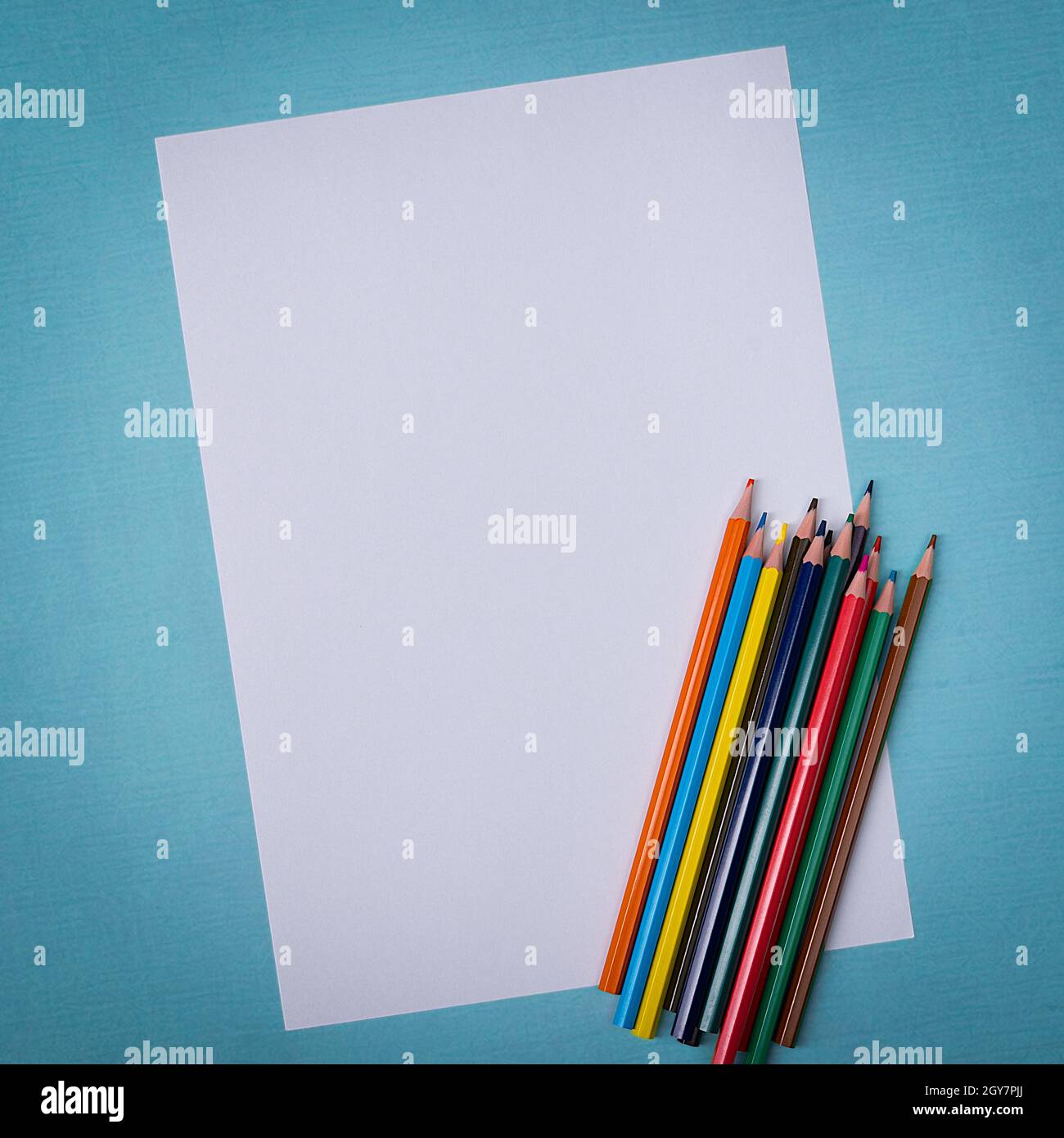 A blank white sheet and colored pencils for drawing on a plain textured ...
