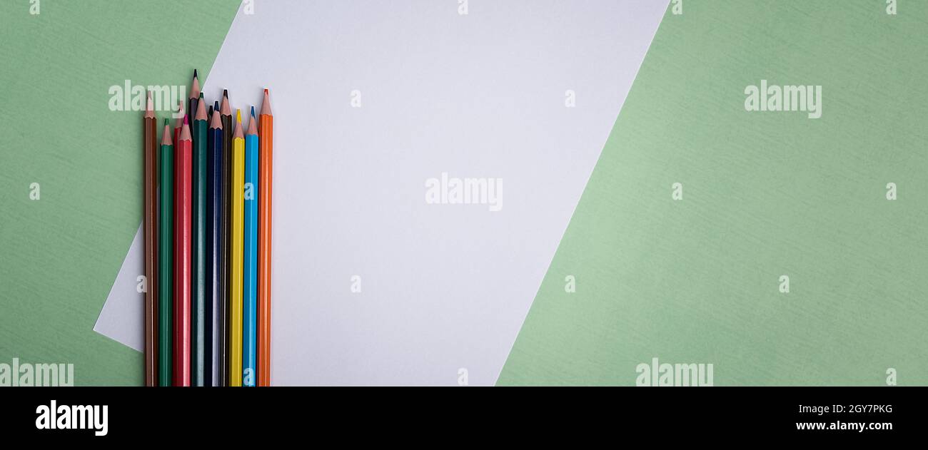 A blank white sheet and colored pencils for drawing on a plain textured ...