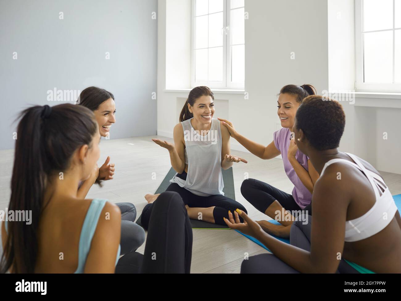 Smiling female yoga class members relax and talk while sitting on the ...