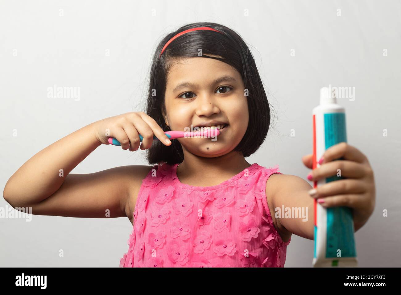 Portrait of an Indian girl child brushing teeth with toothbrush and holding toothpaste tube on ...