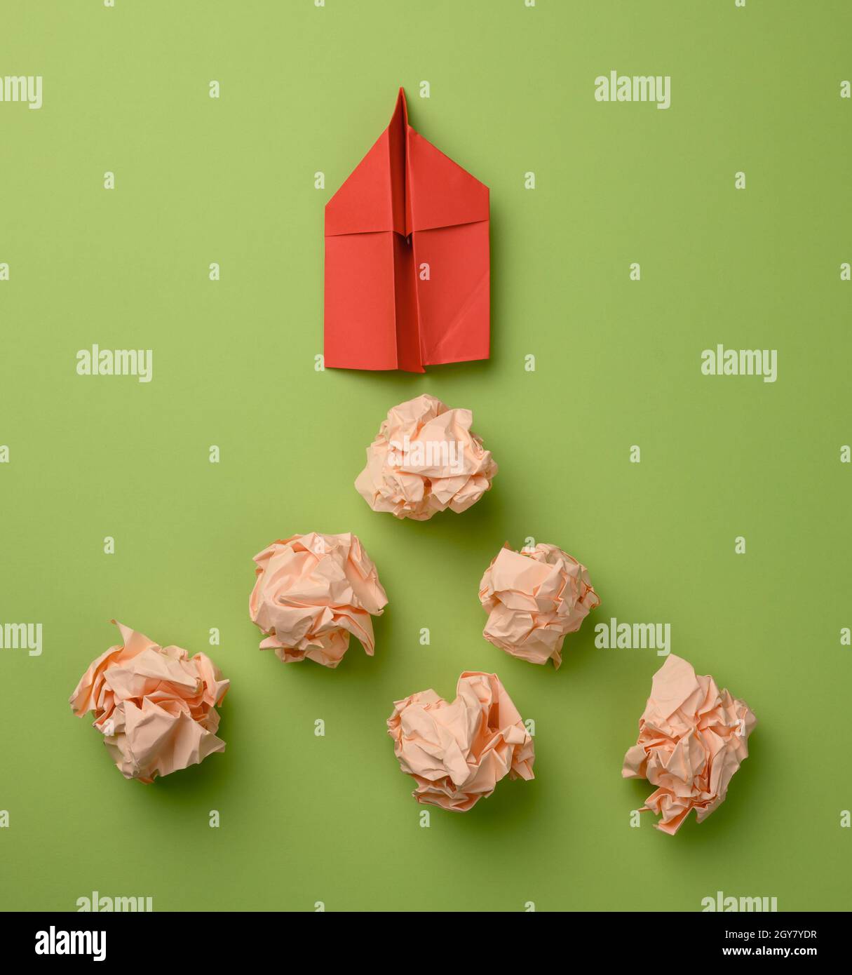 red paper airplane and crumpled paper balls on a green background, top ...