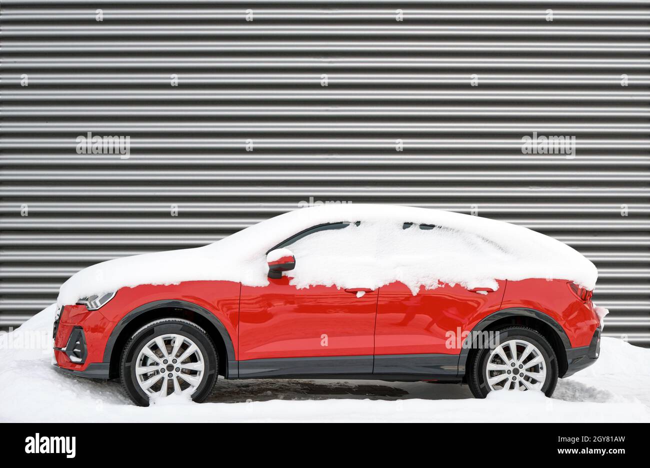 Modern red car covered in snow in winter against corrugated metal wall ...