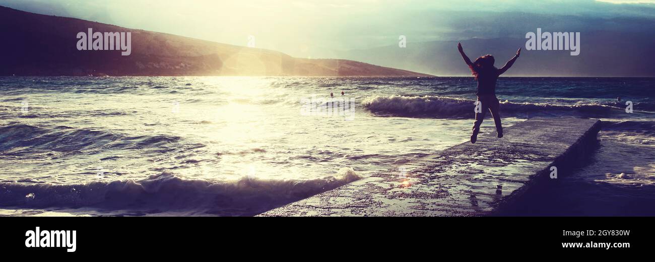 Feeling of freedom concept. Woman jump on pier facing to the sea with ...