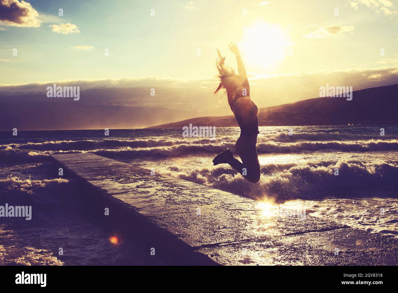 Feeling of freedom concept. Woman jump on pier facing to the sea with ...