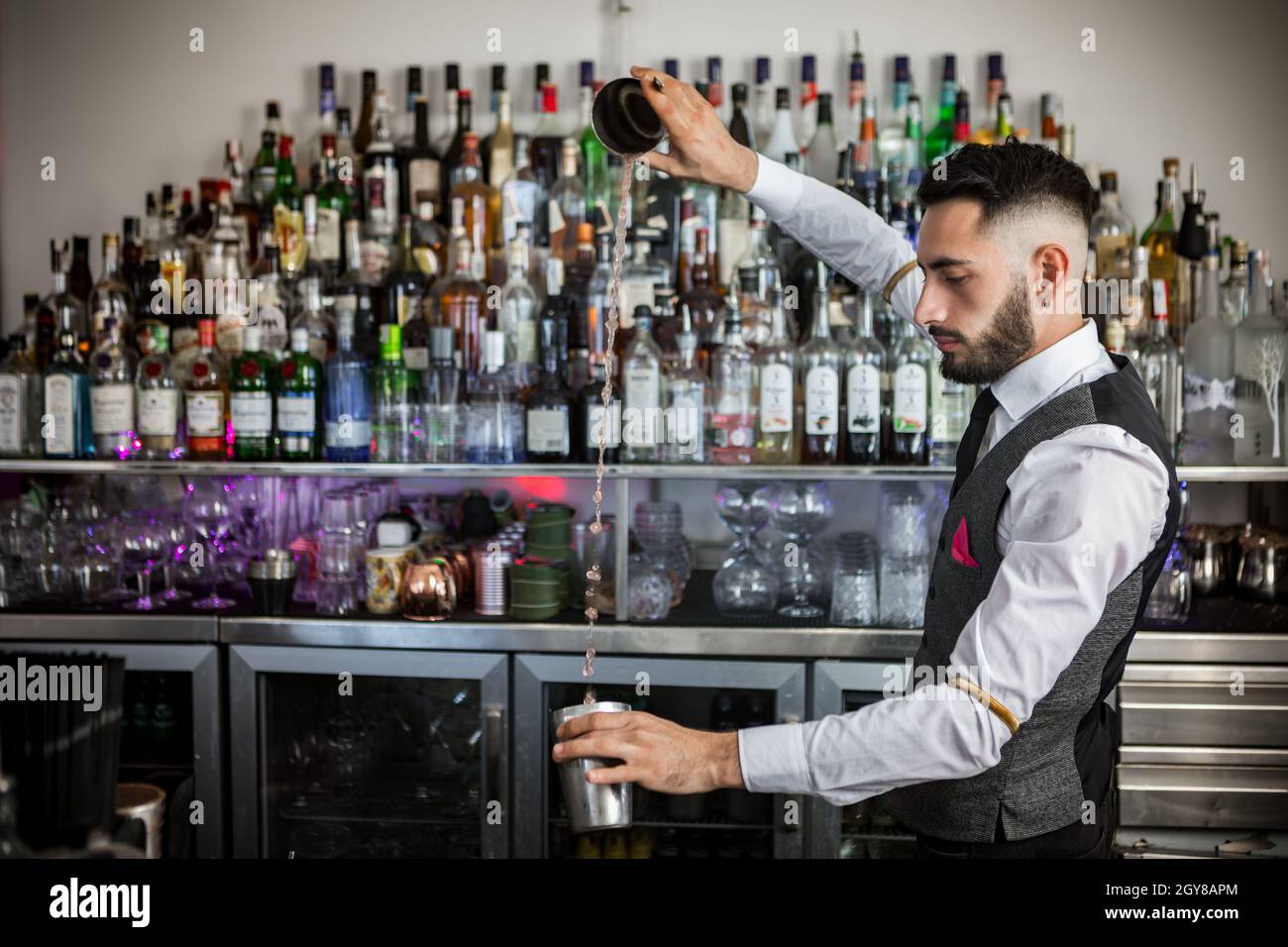 Side view of young bearded male barkeeper in elegant uniform pouring ...