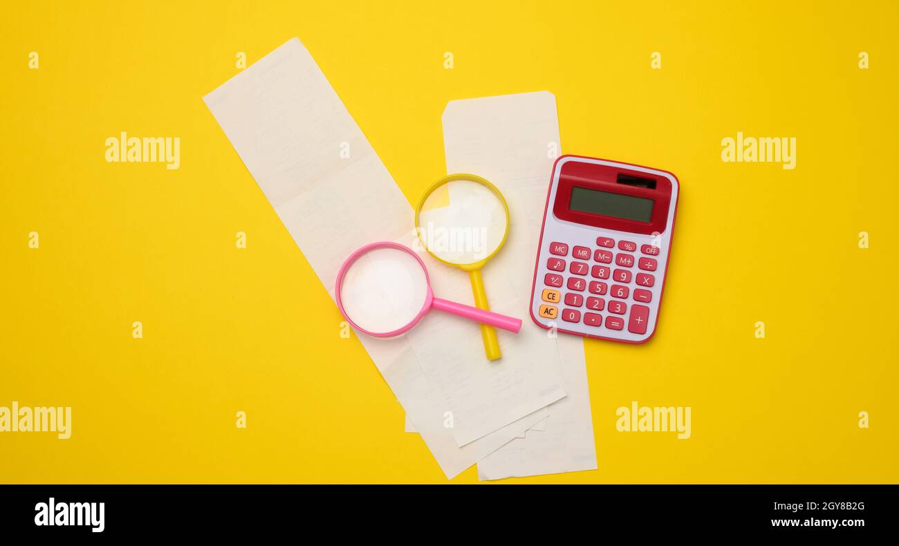 a stack of paper checks, a pink plastic calculator and a magnifying ...