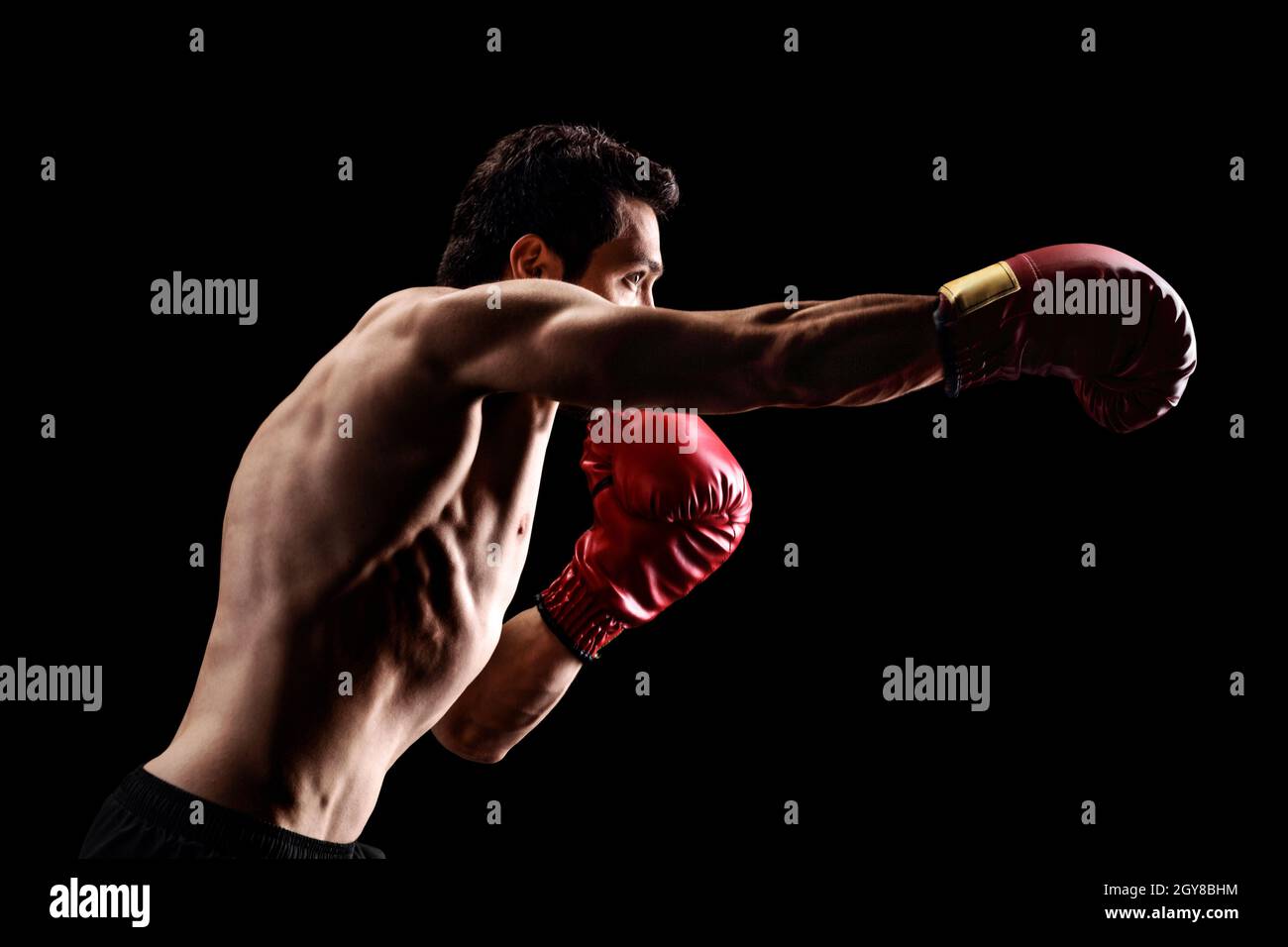Strong young man punching with boxing gloves on a black background ...