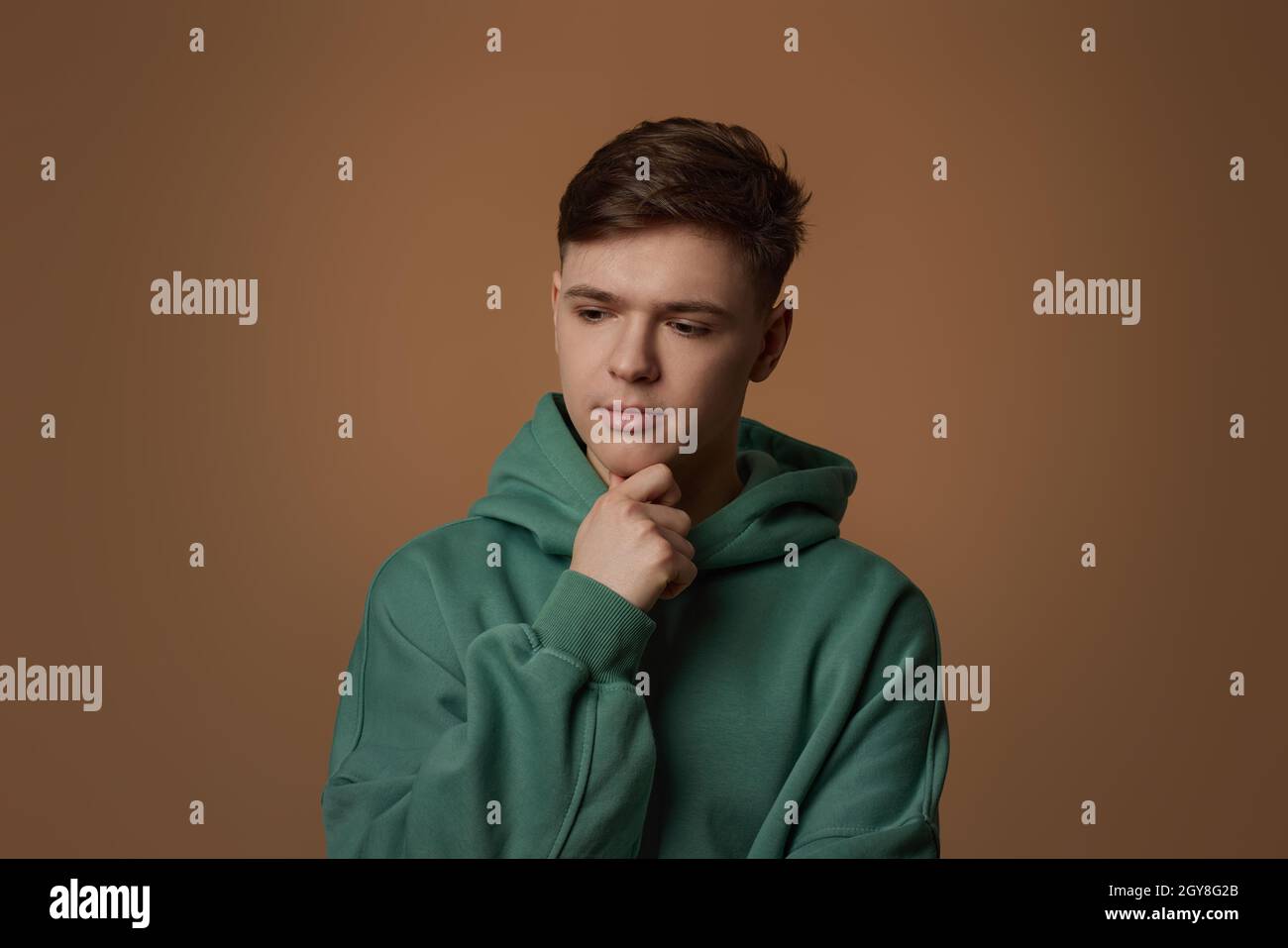 young handsome guy touch his chin by hand thinking isolated on brown ...