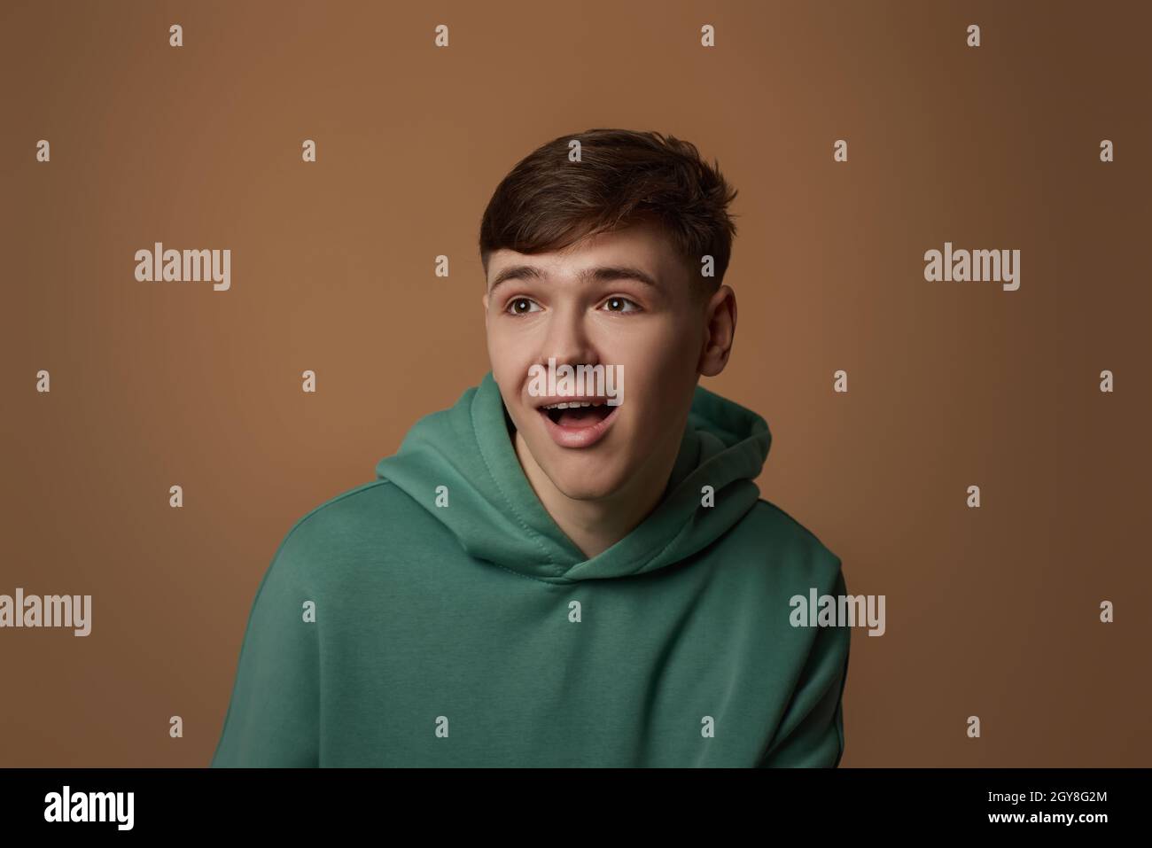 surprised young handsome guy in sweatshirt isolated on brown background ...