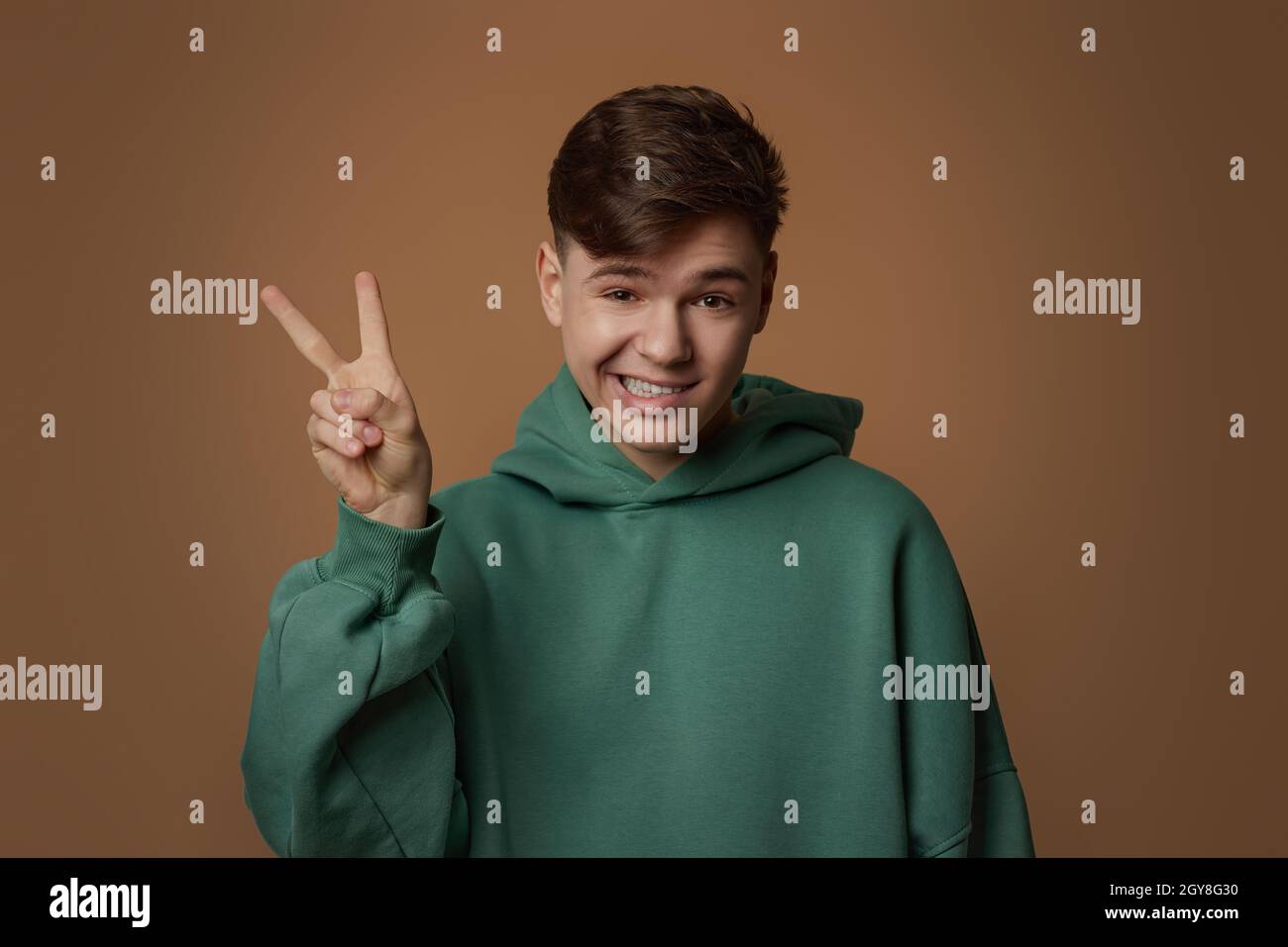 young handsome guy in sweatshirt showing victory gesture isolated on ...