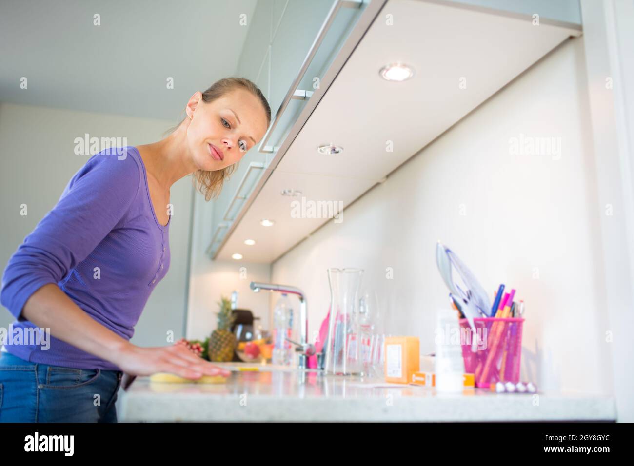 Pretty, young woman cleaning her modern kitchen after cooking lunch ...